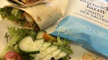 Um prato com um wrap, salada e um saco de batatas fritas Fairfield Farm levemente salgadas.