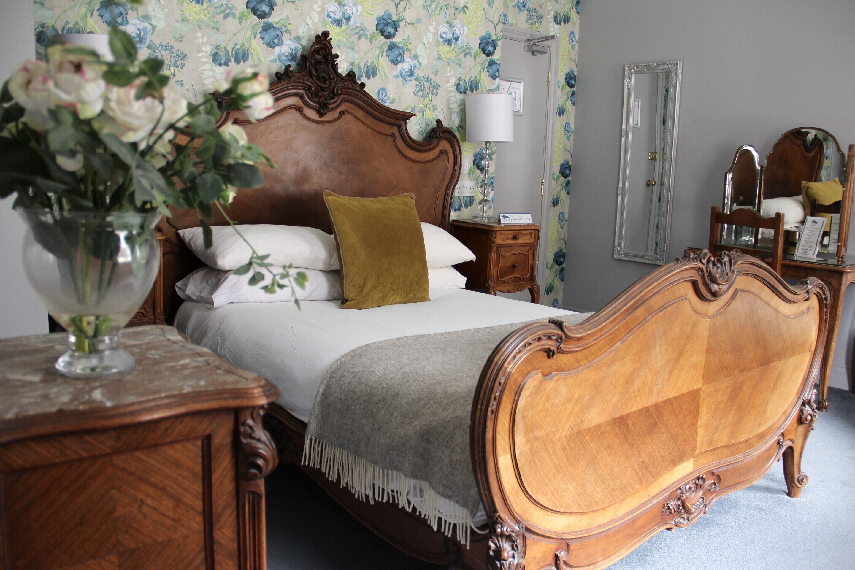 Quarto com cama de madeira, mesa de cabeceira, espelho e papel de parede floral.