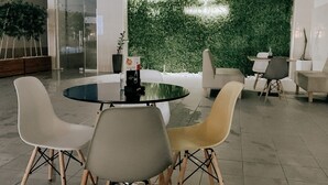 Uma sala de reuniões moderna com uma mesa de vidro redonda, quatro cadeiras com pernas de madeira, uma parede verde com planta trepadeira e teto de madeira.
