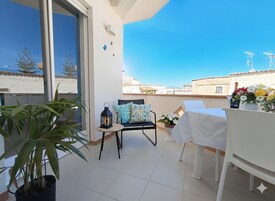 Uma varanda com mesa, cadeiras, um vaso de planta e vista para prédios.