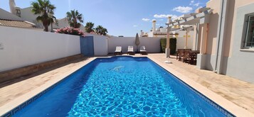 Piscina com borda azulejada, rodeada por um muro branco e uma pérgula.