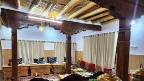 Quarto tradicional com teto de madeira, área de estar central com almofadas e uma mesa posta para refeições.