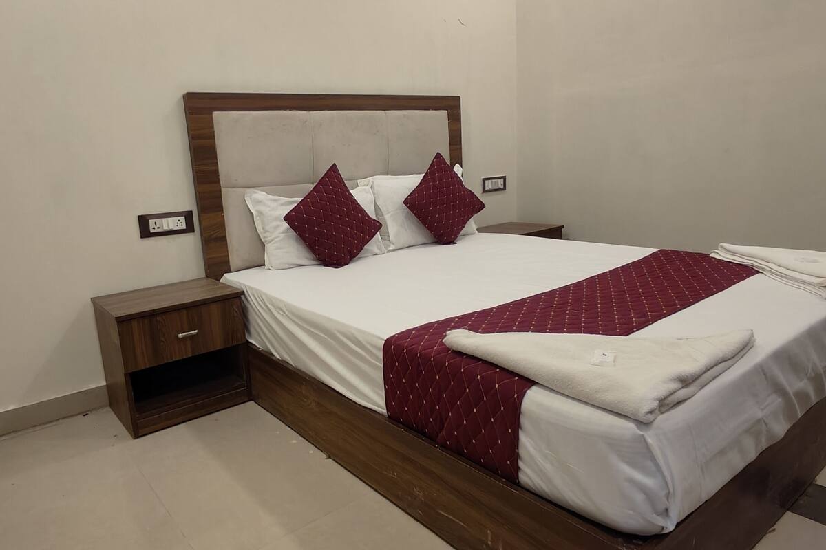 Uma cama bem arrumada com cabeceira de madeira, duas mesas de cabeceira e um edredom com padrão vermelho e branco.
