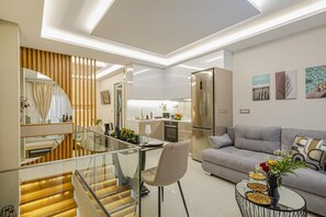 Uma sala de estar moderna com um sofá cinzento, uma mesa de centro de vidro com objetos decorativos e uma escada com guarda-corpo de madeira.