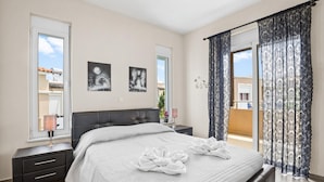 Um quarto com cama, mesas de cabeceira, janela com cortinas e uma obra de arte na parede.