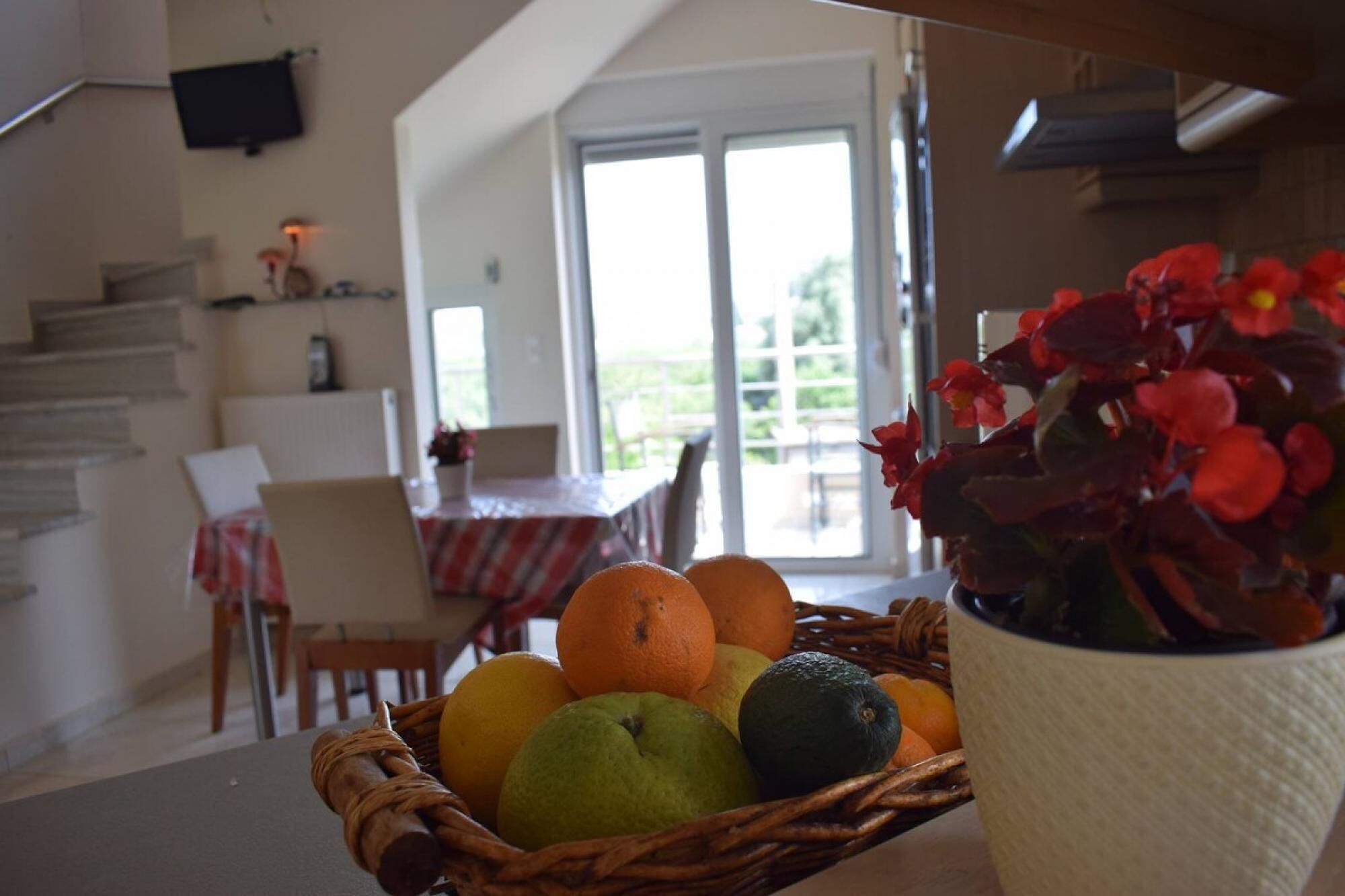 Uma sala de jantar com mesa e cadeiras, uma cesta de vime com frutas e um vaso de planta.