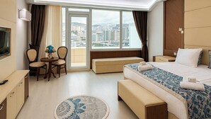 Quarto de hotel moderno com uma cama grande, uma mesa, uma cadeira e vista para a cidade.