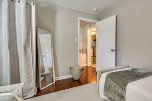 Um quarto com cama, espelho, porta e corredor que dá para uma cozinha.