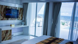 Quarto de hotel moderno com uma cama grande, televisão montada e varanda com vista para a piscina.