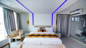 Quarto de hotel moderno com uma cama grande, mesas de cabeceira, um espaço de estar e um banheiro.