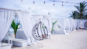 Uma área de descanso à beira-mar com toldos brancos, cadeiras suspensas e luzes de Natal.