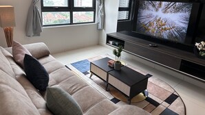 Uma sala de estar moderna com uma televisão de tela grande, um sofá, uma mesa de centro e vista para o horizonte da cidade através de uma janela.
