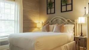 Uma cama bem arrumada com lençóis brancos, cabeceira de madeira e duas luminárias fixadas na parede.