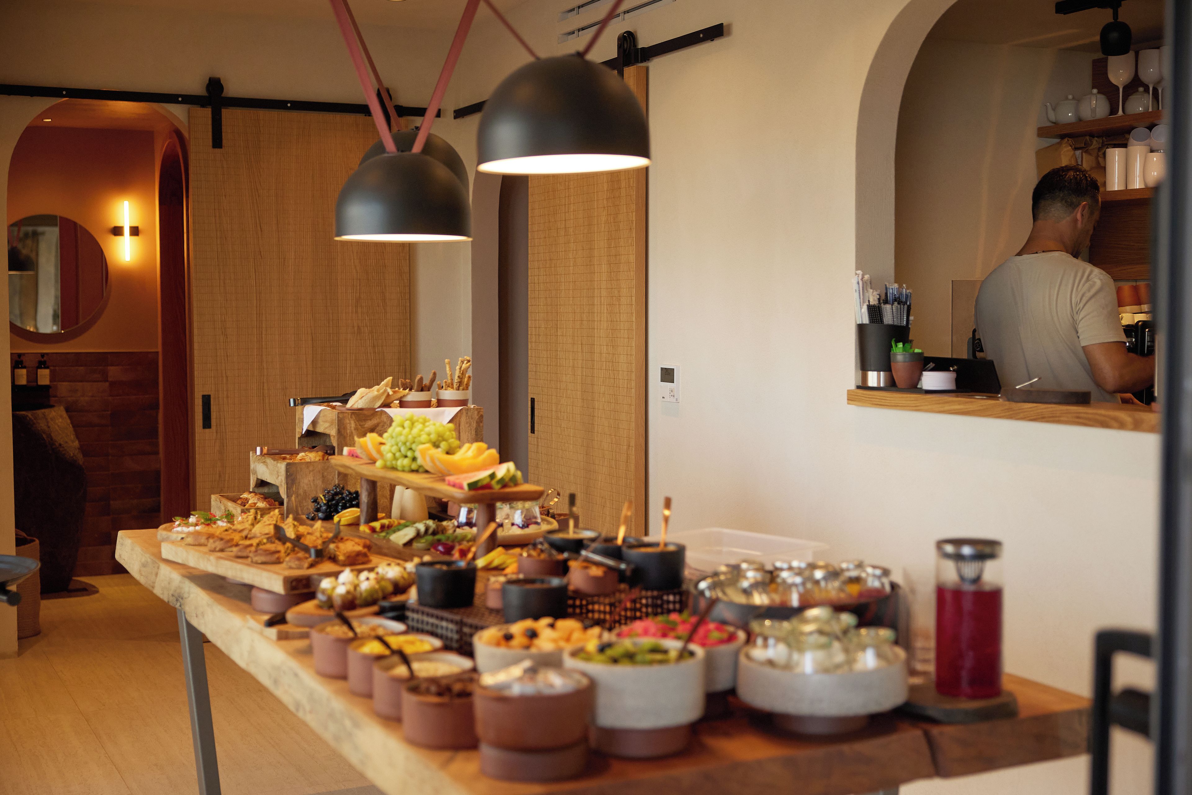 Mesa de buffet com diversos alimentos e uma pessoa ao fundo.