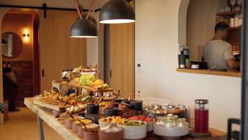 Mesa de buffet com diversos alimentos e uma pessoa ao fundo.