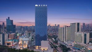Um hotel moderno com fachada de vidro, rodeado por outros edifícios e uma rua movimentada abaixo.