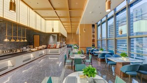 Um hall de hotel moderno com um balcão comprido, área de estar e grandes janelas com vista para a cidade.