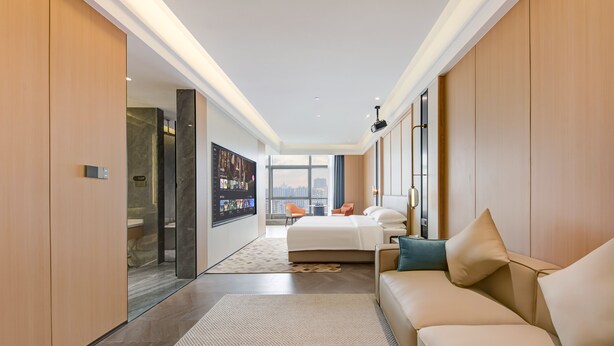 Quarto de hotel moderno com uma cama grande, um sofá, uma TV e vista para a cidade.