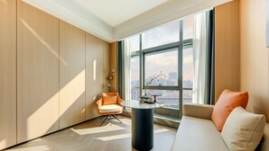 Uma sala de estar moderna com uma janela grande, um sofá, uma poltrona e uma mesa pequena.