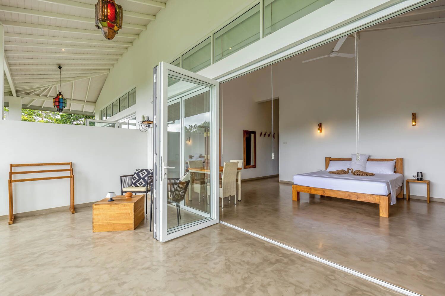 Quarto moderno com uma cama grande, uma mesinha de cabeceira de madeira, uma cadeira e uma pequena mesa.