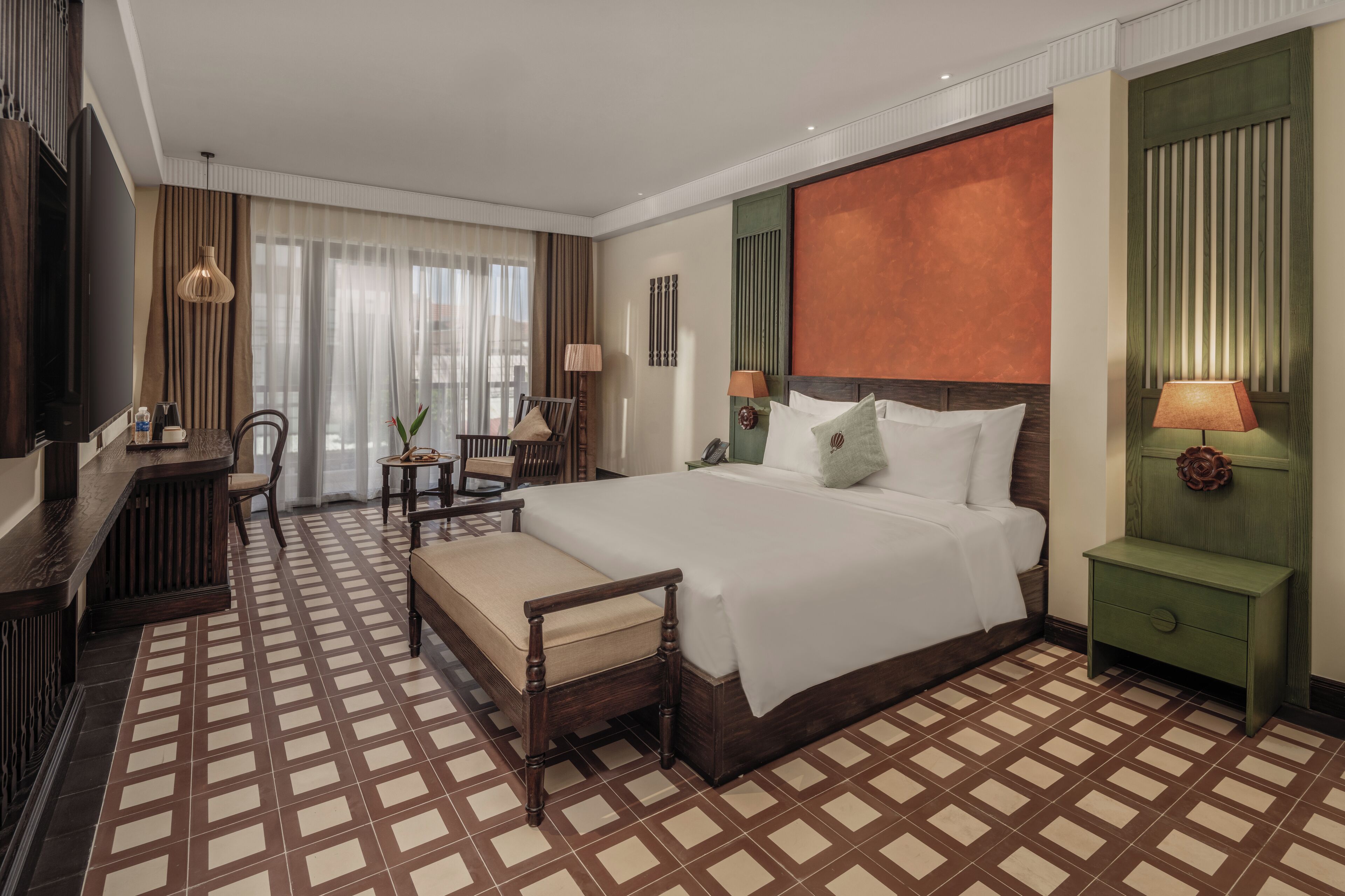 Quarto de hotel com uma cama grande, uma escrivaninha, uma cadeira, uma televisão e uma luminária.