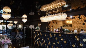 Uma área de recepção de hotel com design moderno, apresentando um balcão de atendimento, espaço para assentos e iluminação decorativa.