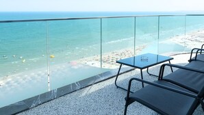 Varanda com guarda-corpo de vidro com vista para uma praia com pessoas e guarda-sóis.