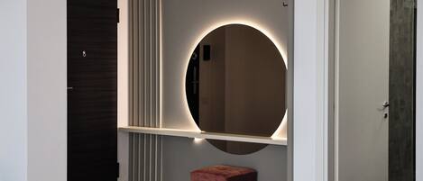 Um interior moderno com uma porta escura, um espelho redondo com um brilho luminoso e um banquinho vermelho.