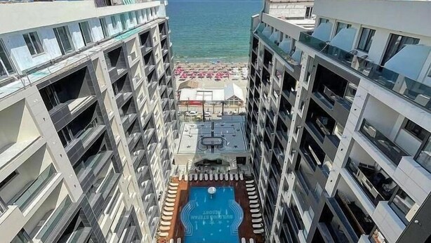 Um hotel moderno com piscina central, várias varandas e vista para a praia.