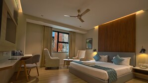 Quarto de hotel moderno com uma cama grande, duas poltronas, uma escrivaninha e um ventilador de teto.