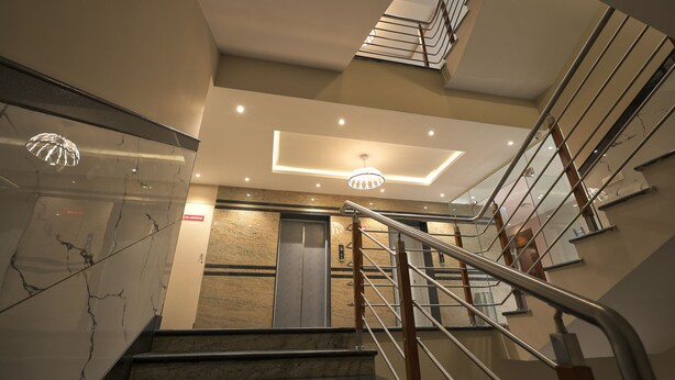 Interior moderno de hotel com escadaria de mármore, elevador de vidro e luminárias contemporâneas.