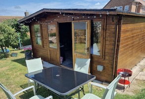 Uma cabana de madeira com porta de vidro, uma mesa e cadeiras na parte externa.