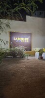 Uma entrada pavimentada com uma placa indicando 'LA ROSELINE' e uma parede com uma janela.