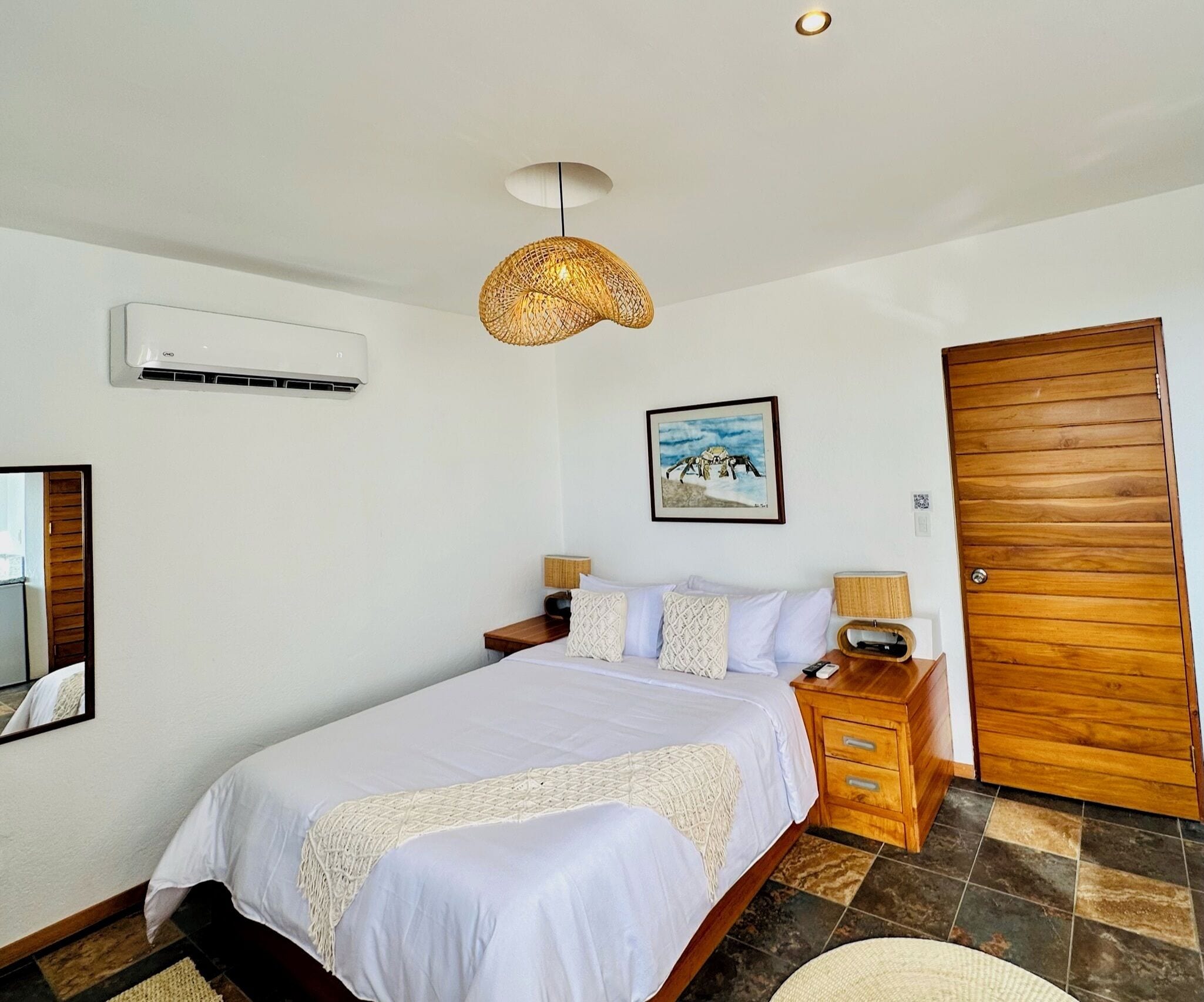 Quarto com cama, mesas de cabeceira, porta de madeira e luminária no teto.