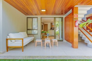 Interior moderno com teto de madeira, um sofá branco, uma mesa pequena com bancos e uma escada com corrimão de madeira.