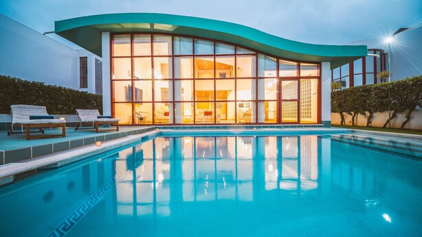 Um edifício moderno com grandes janelas de vidro, piscina e cadeiras de descanso.