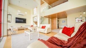 Uma sala de estar espaçosa com pé direito alto, TV de tela plana e um ambiente acolhedor para sentar.