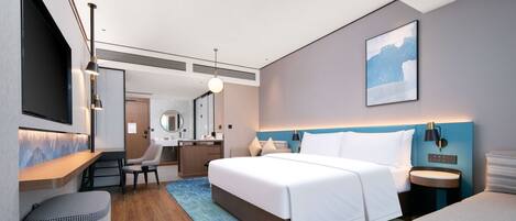 Quarto de hotel moderno com uma cama grande, uma escrivaninha, uma cadeira e um pequeno banquinho.
