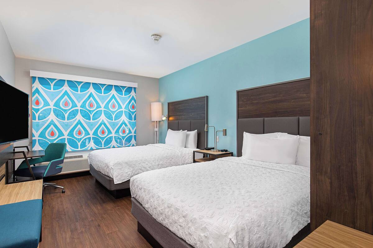 Quarto de hotel com duas camas, uma escrivaninha, uma cadeira e uma televisão.