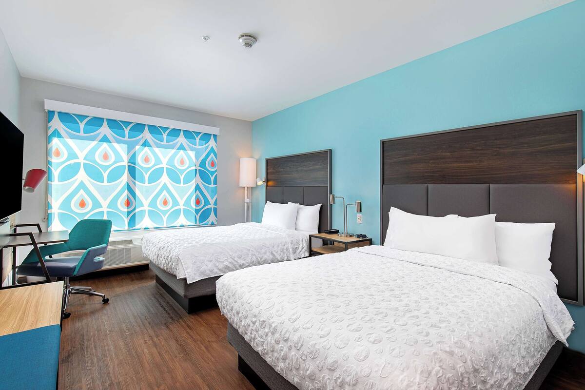 Quarto de hotel com duas camas, uma mesa, uma cadeira e uma televisão.