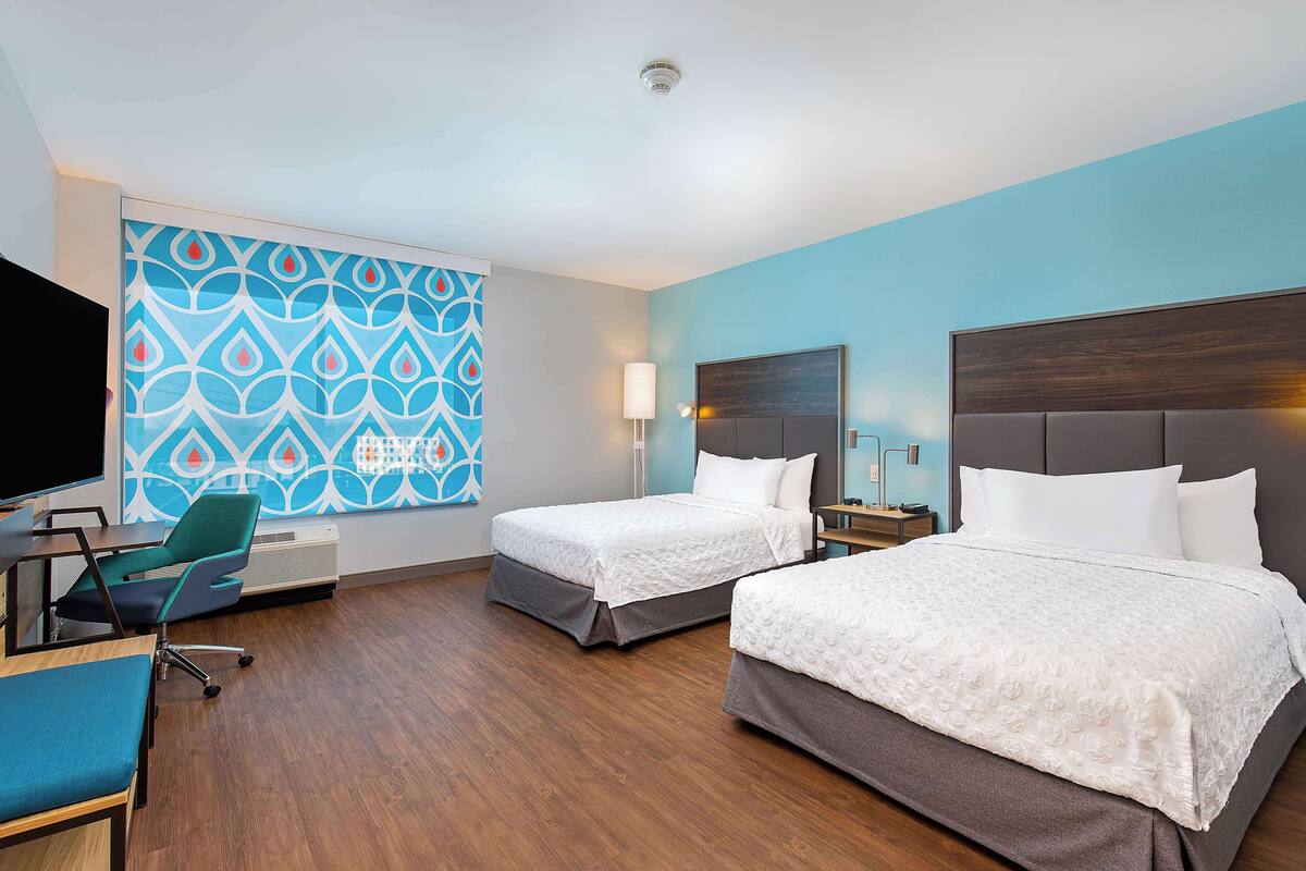 Quarto de hotel com duas camas, uma mesa, uma cadeira e uma televisão.