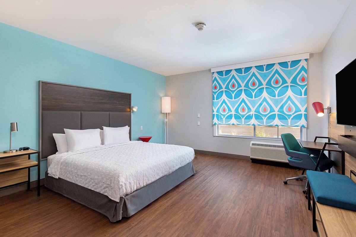 Quarto de hotel moderno com uma cama grande, uma escrivaninha, uma cadeira e uma televisão.