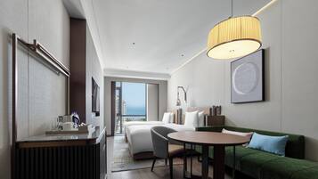 Quarto de hotel moderno com cama, escrivaninha, sofá verde e mesa de jantar.