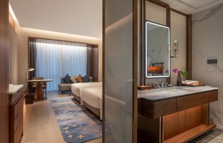 Quarto de hotel com cama, mesa de cabeceira, luminária e um espelho grande.