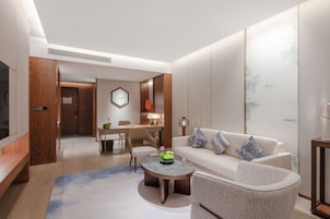 Quarto de hotel moderno com sofá, poltrona, mesinha de centro e escrivaninha com luminária.