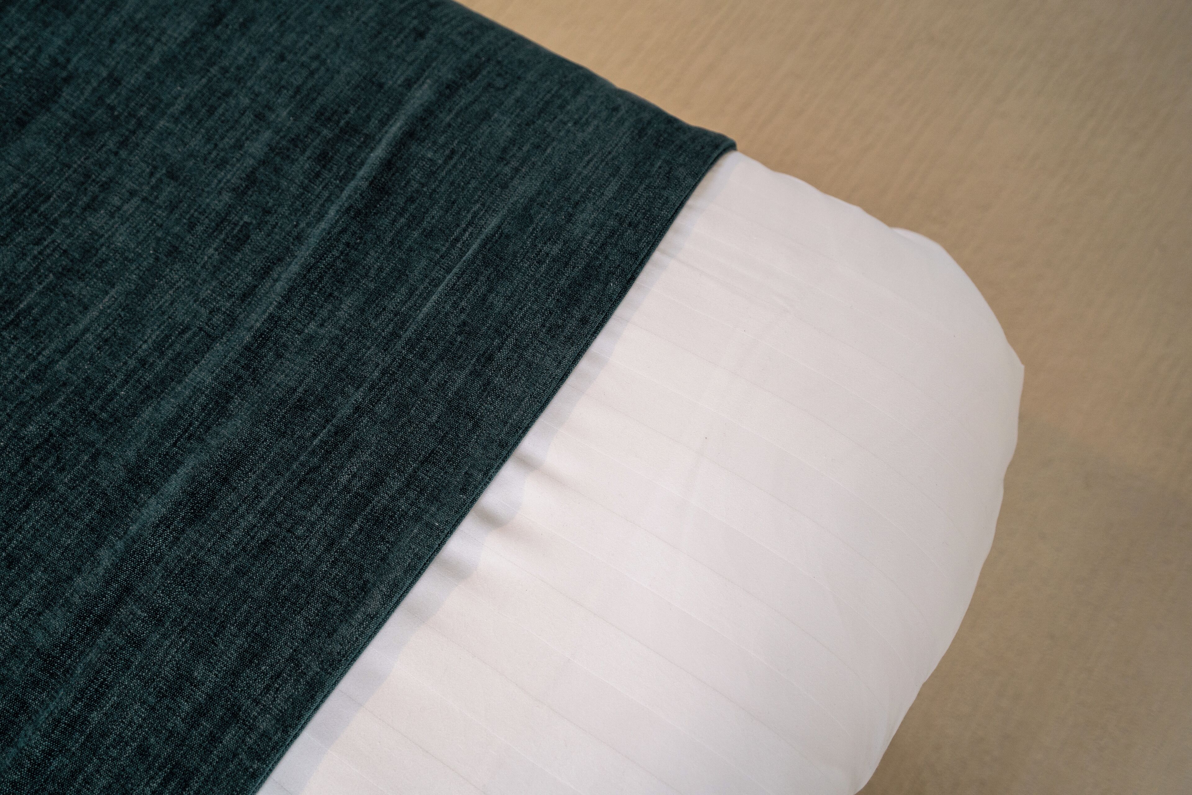 Uma cama com um cobertor verde escuro e um travesseiro branco.