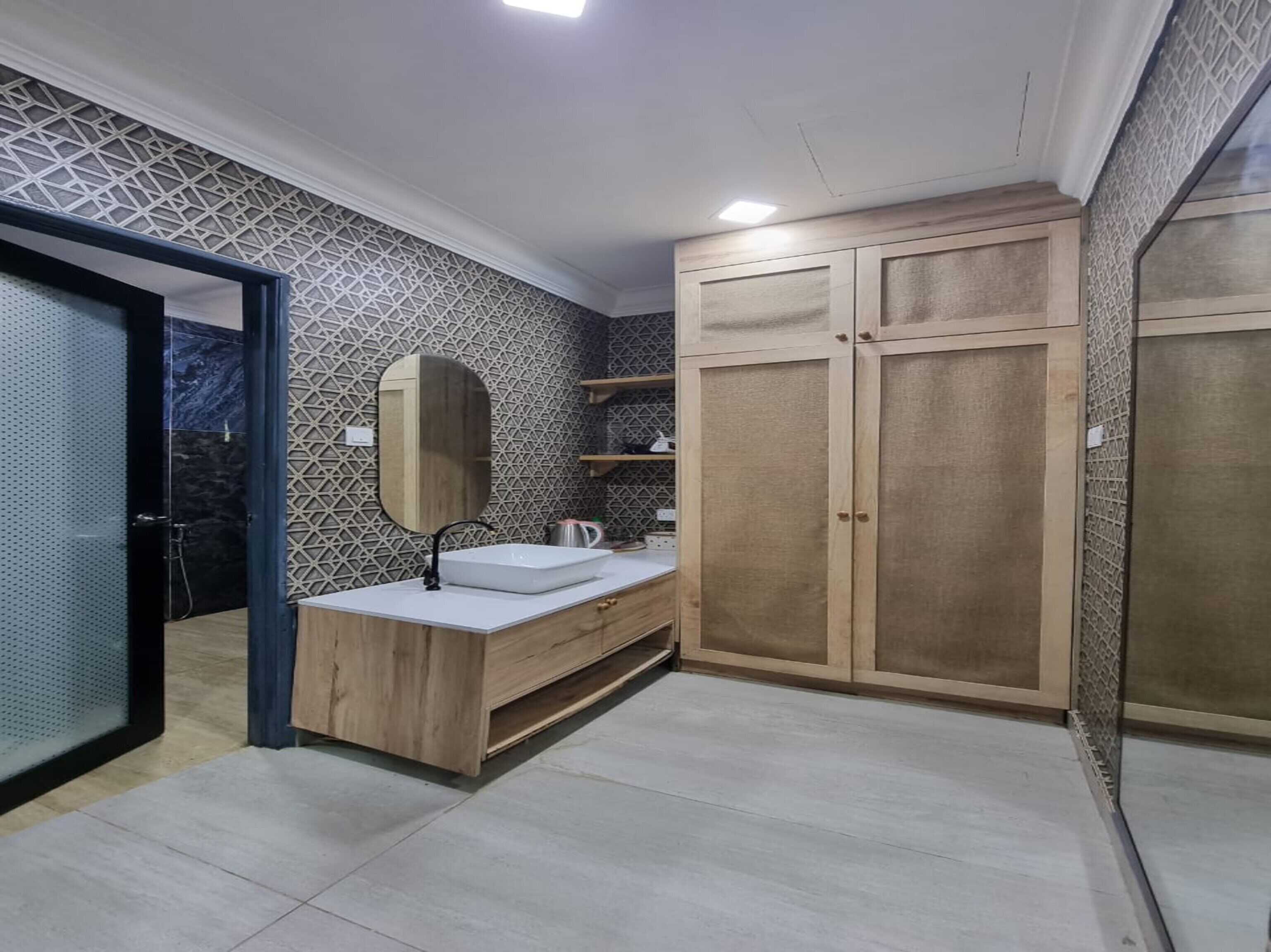 Casa de banho com toucador de madeira, lavatório branco e espelho. Tem zona de duche com porta de vidro e chão em mosaicos.