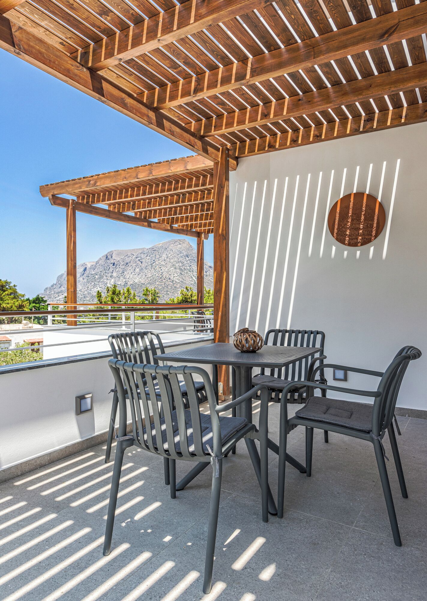 Um pátio externo com pérgola, uma mesa com cadeiras e vista para montanhas.