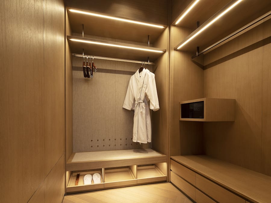 Um closet amplo e moderno, bem iluminado, com paredes de madeira, um banco e um cabideiro.