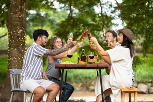 Um grupo de pessoas brindando com espetinhos e copos de vinho em uma mesa ao ar livre, com vista para o verde.